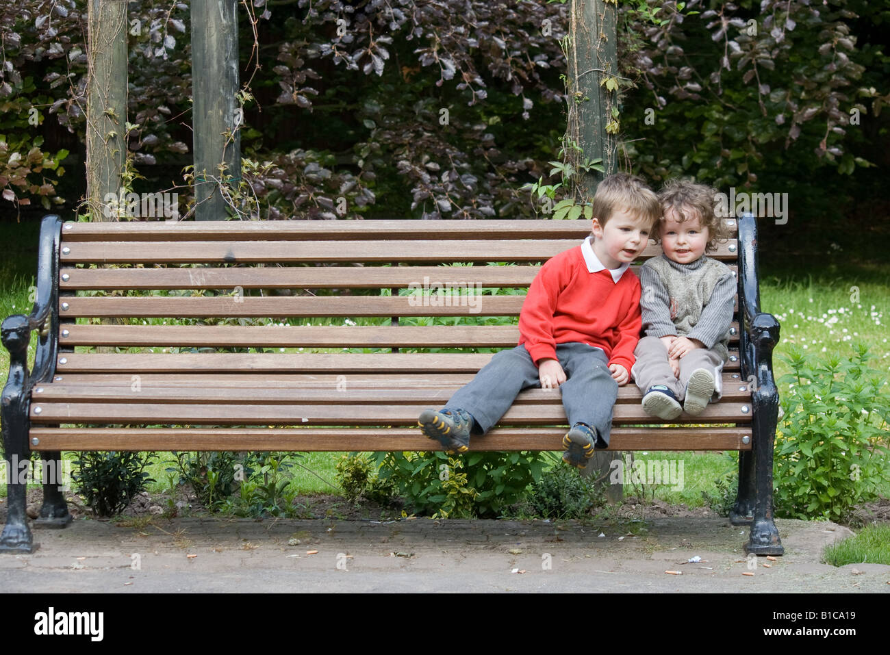 Two small boys sitting on the edge of a park bench Stock Photo - Alamy