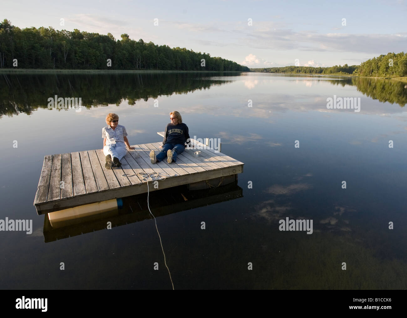 Detached and Chatting. Two women chat while relaxing on a floating dock ...