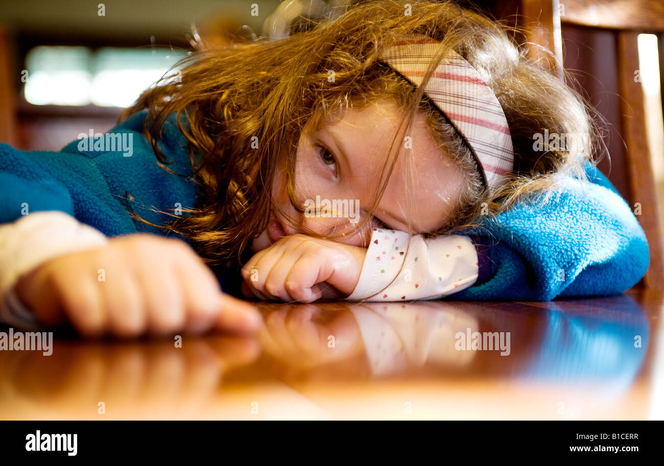A young girl rests her head on the dining room table after a long day ...