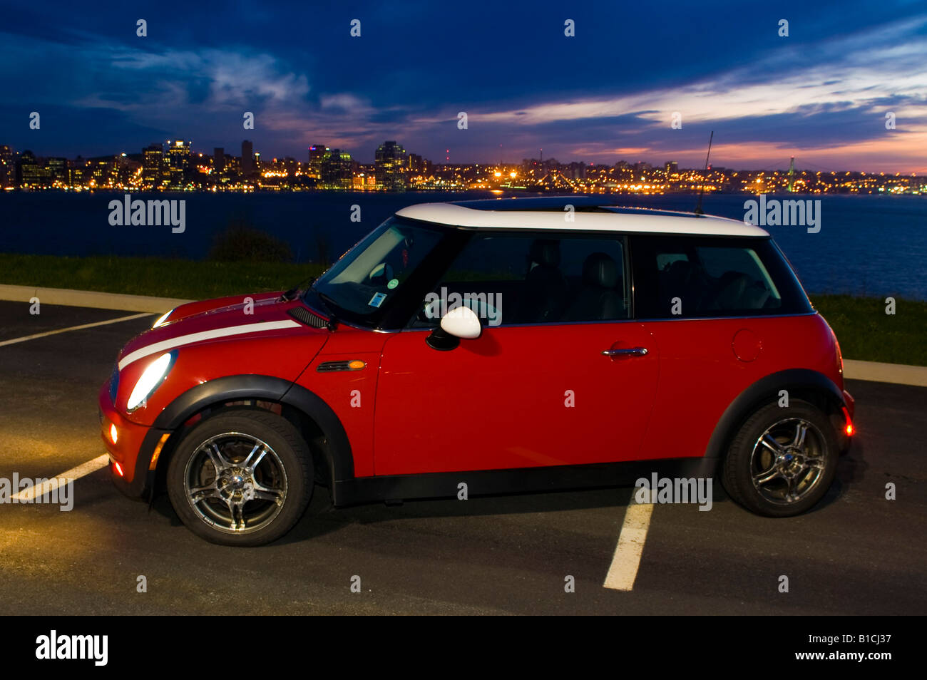 A Mini Cooper, with lights on, taken at dusk set against the backdrop ...