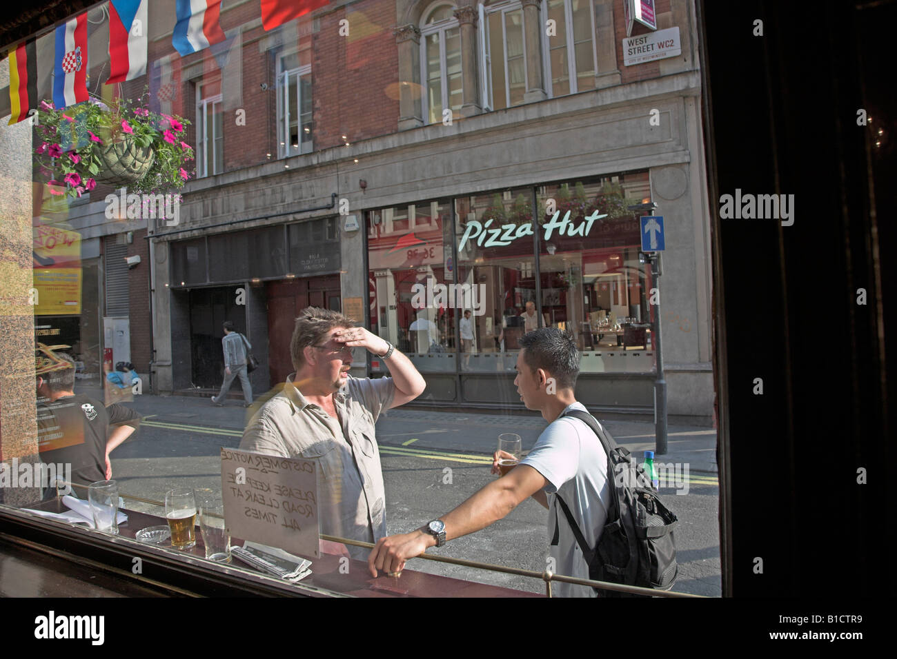 Two men talking on the street outside pub viewed through window from ...