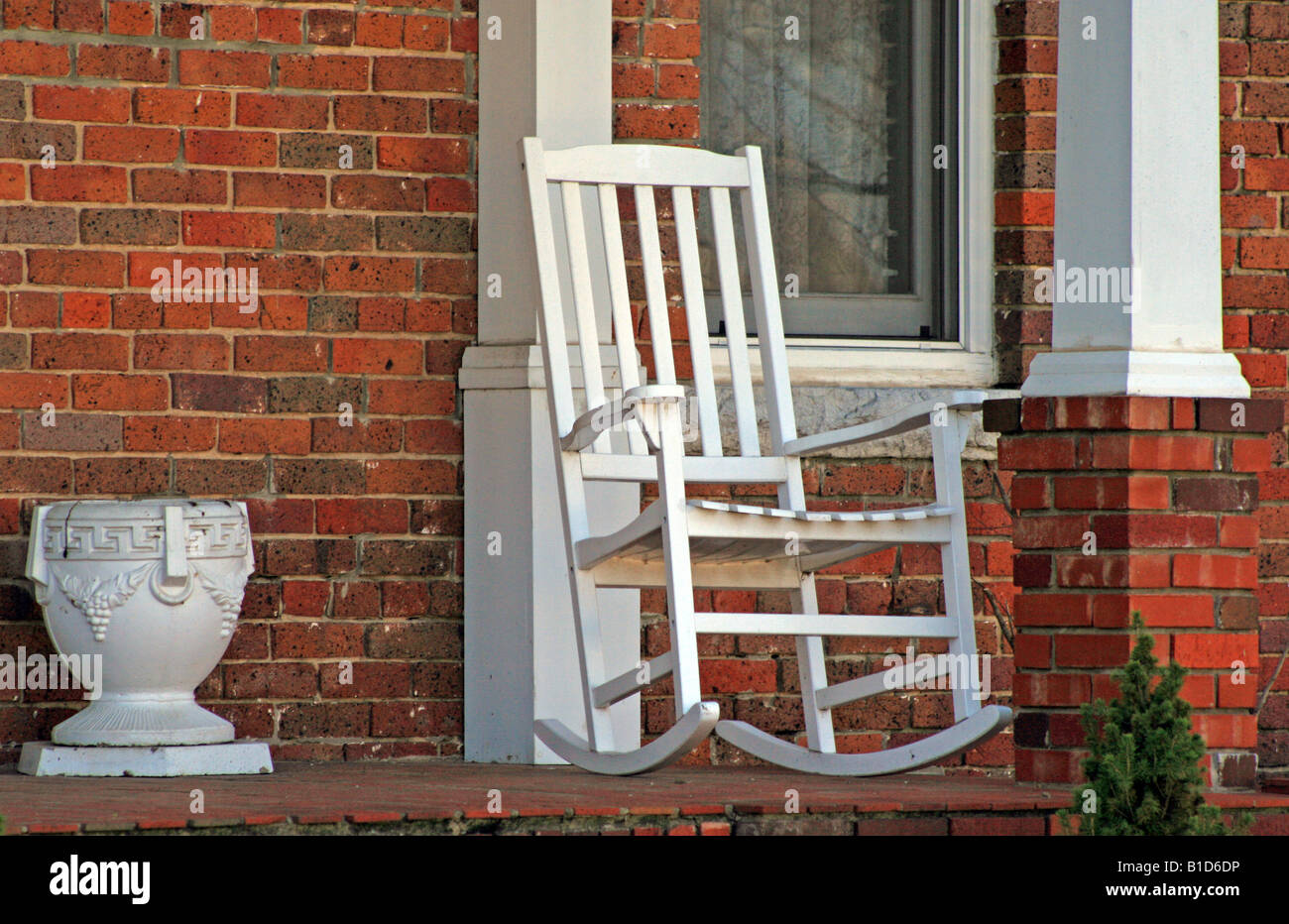 A white rocking chair, planter, and columns on a brick porch Stock ...