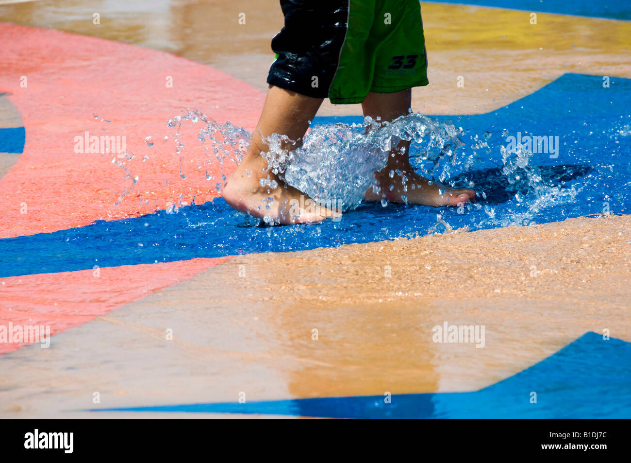 The Feet And Legs Of A 5 To 7 Year Old Boy Standing In A Splash Pad In the-feet-and-legs-of-a-5-to-7-year-old-boy-standing-in-a-splash-pad-in
