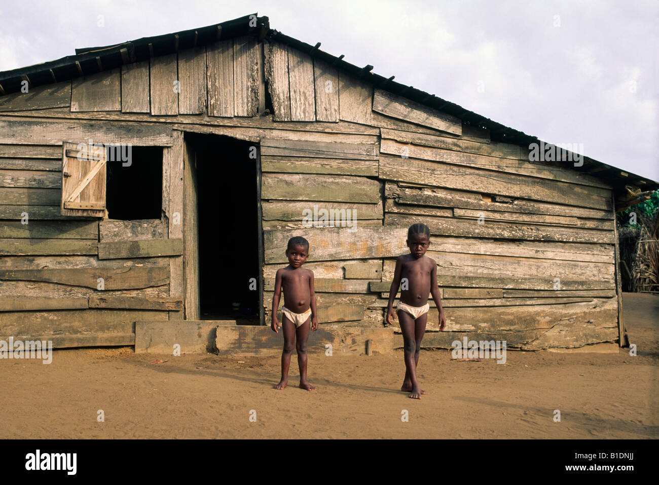 Two children stand in a dusty courtyard in a poor coastal fishing ...
