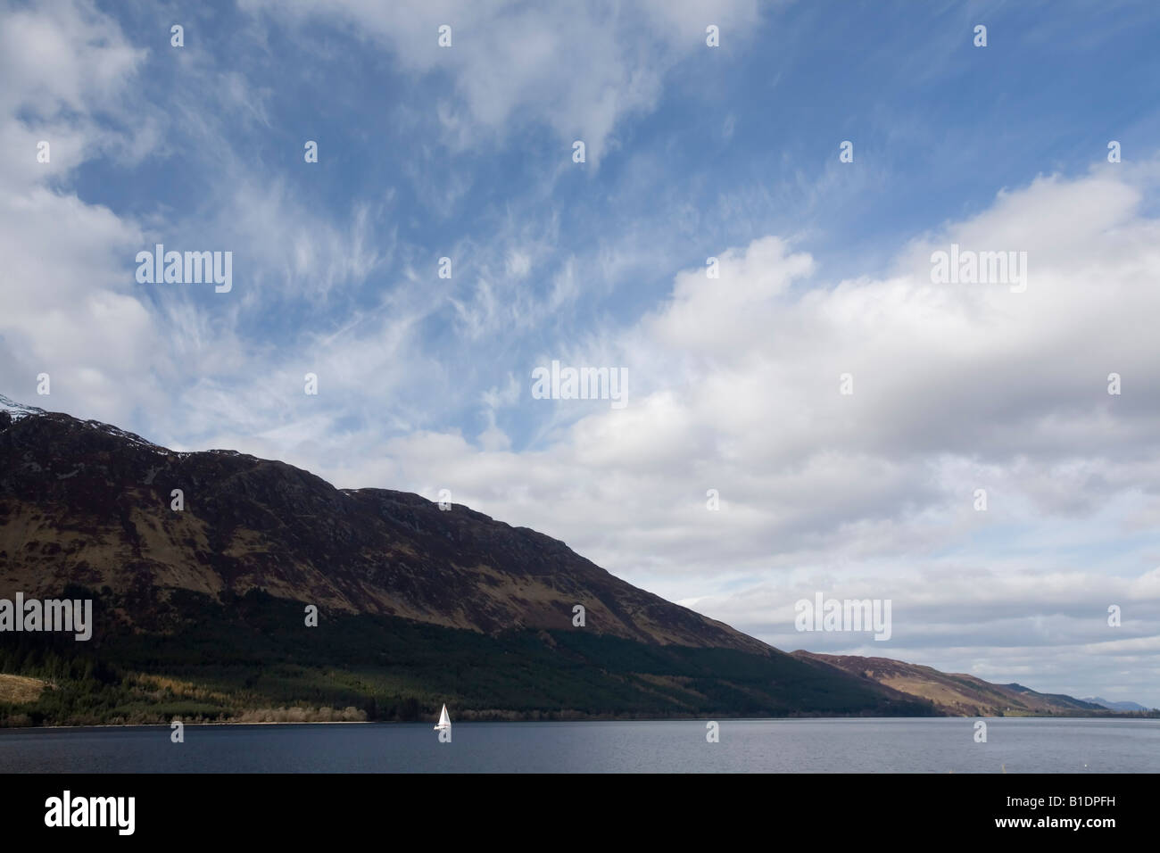A lone sail boat glides through a Scottish Loch as clouds above whisp ...