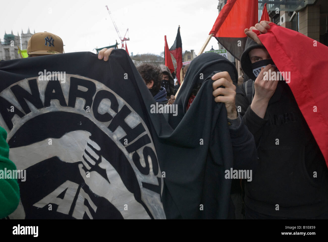 Anarchists with red and black flags and masks at the front of the march ...