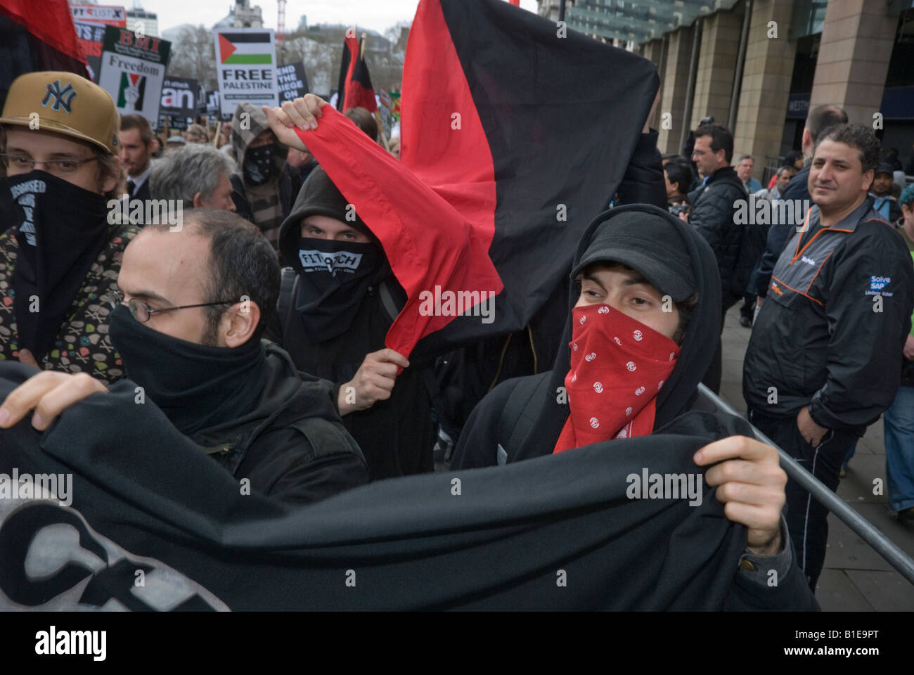 Anarchists with red and black flags and masks at the front of the march ...