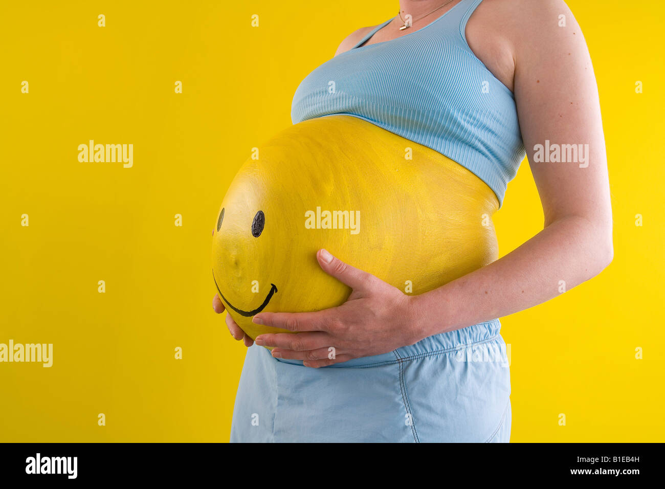 View of pregnant woman's belly with yellow Smiley Face painted on her ...