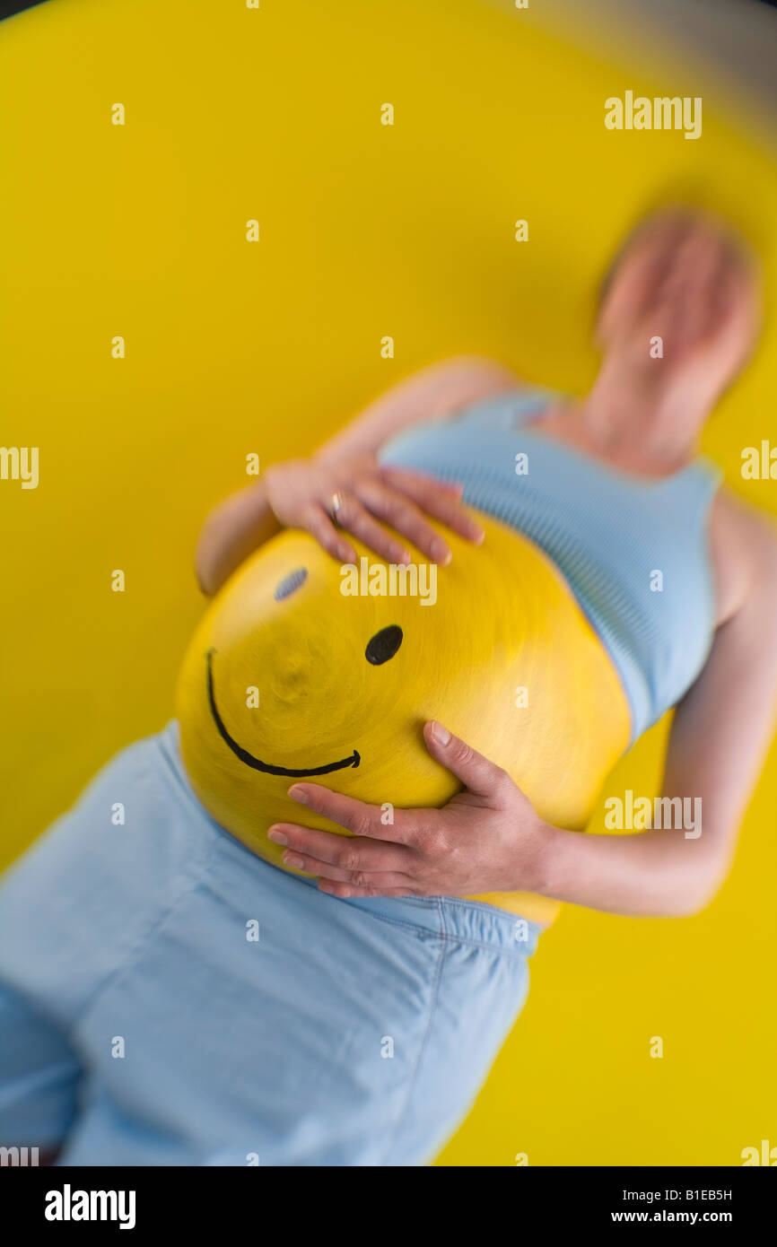 View of pregnant woman's belly with yellow Smiley Face painted on her ...