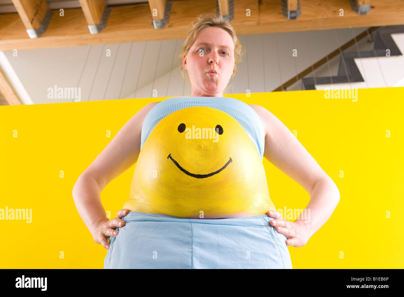 Yellow Smiley Face painted on pregnant woman's stomach as she stands ...
