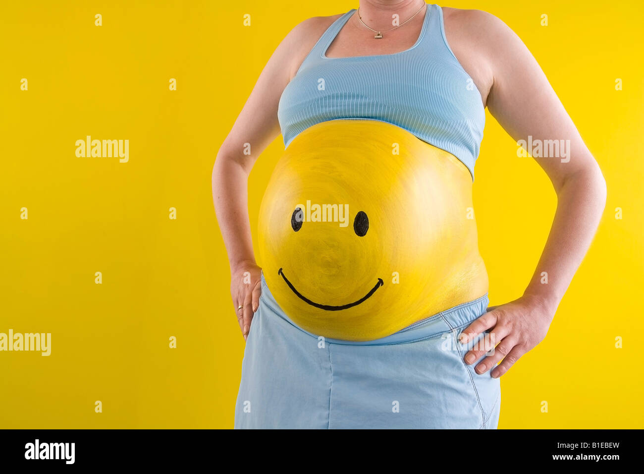 View of pregnant woman's belly with yellow Smiley Face painted on her ...