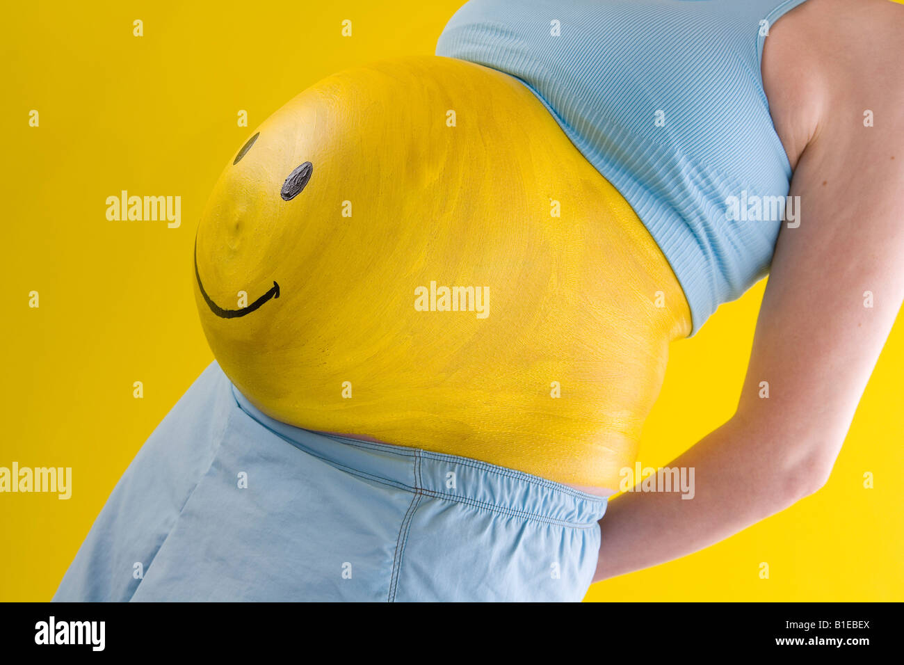 View of pregnant woman's belly with yellow Smiley Face painted on her ...