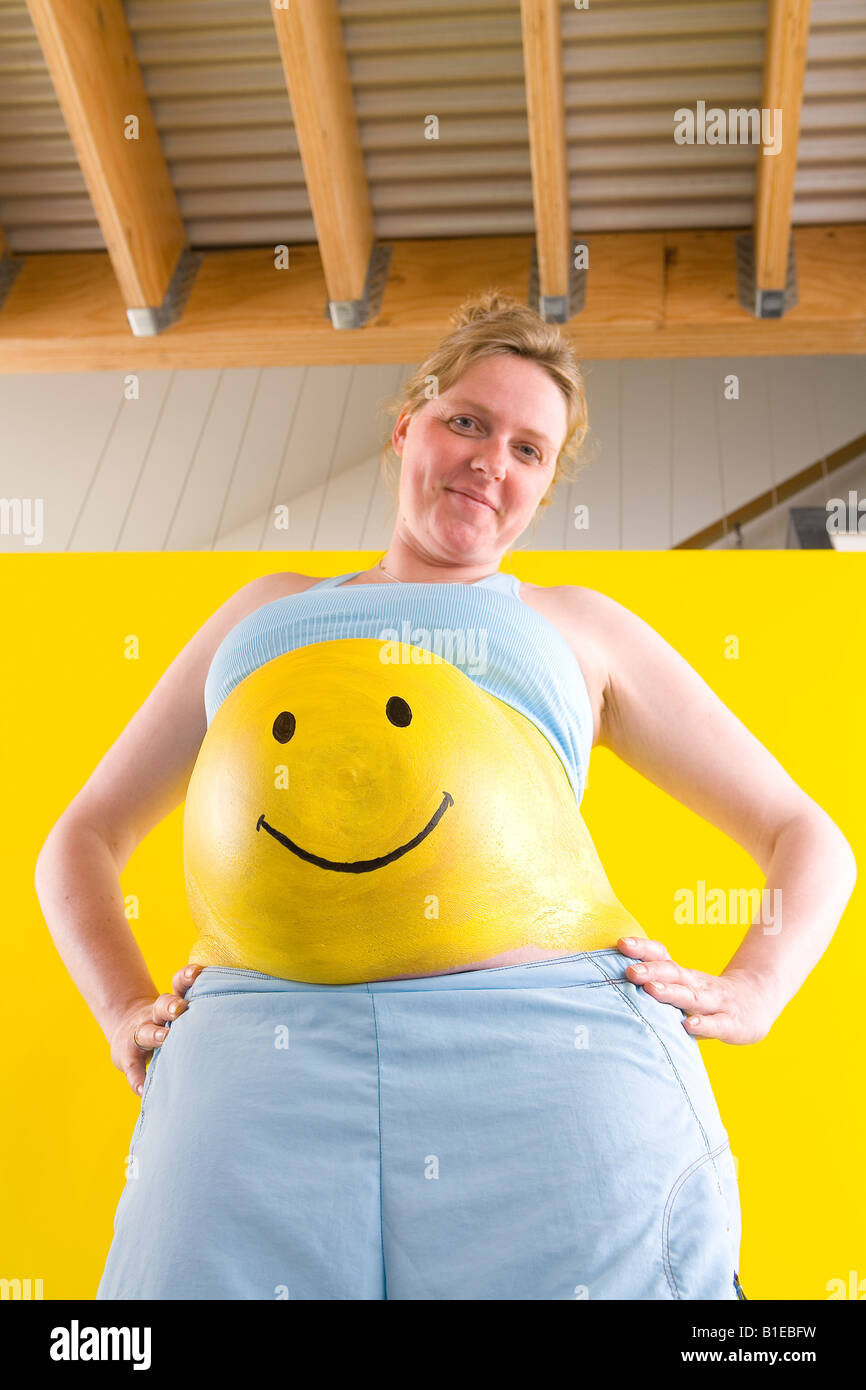 Yellow Smiley Face painted on pregnant woman's stomach as she stands ...