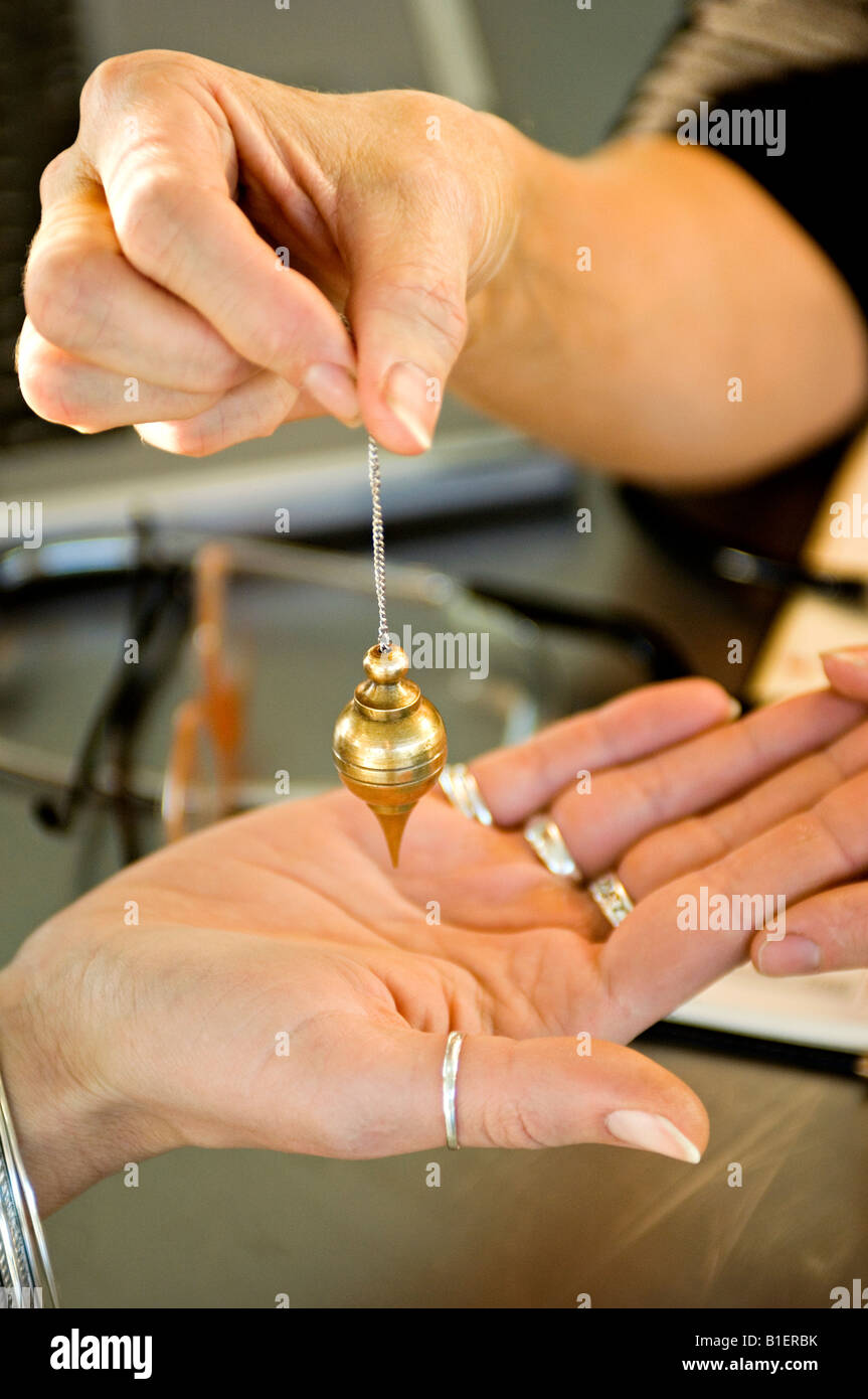 Close-up of a woman's hand holding a dowsing pendulum over a woman's ...