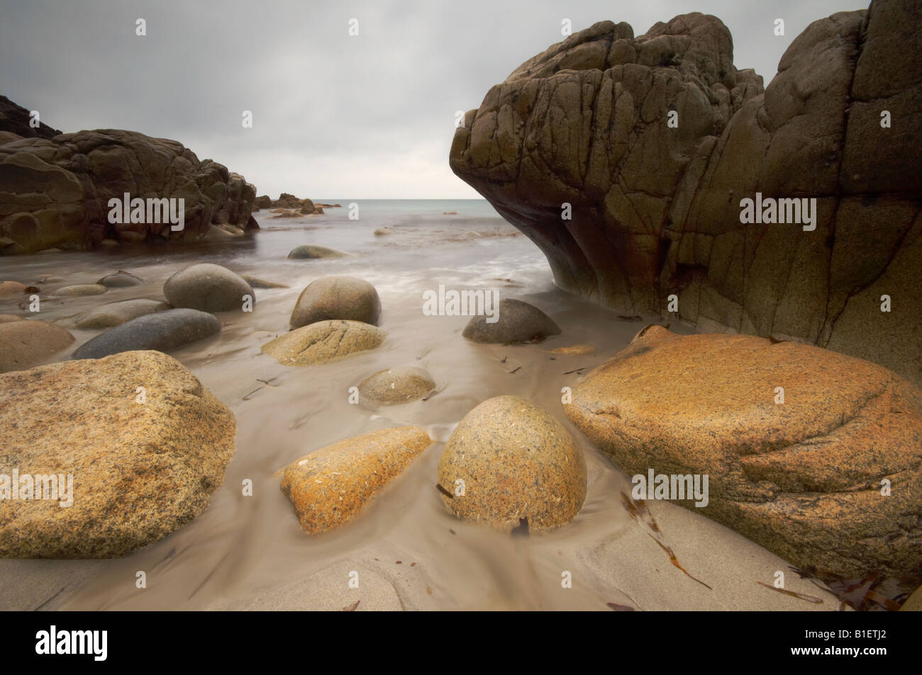 Waves rushing around large boulders on the shoreline of Porth Nanven ...