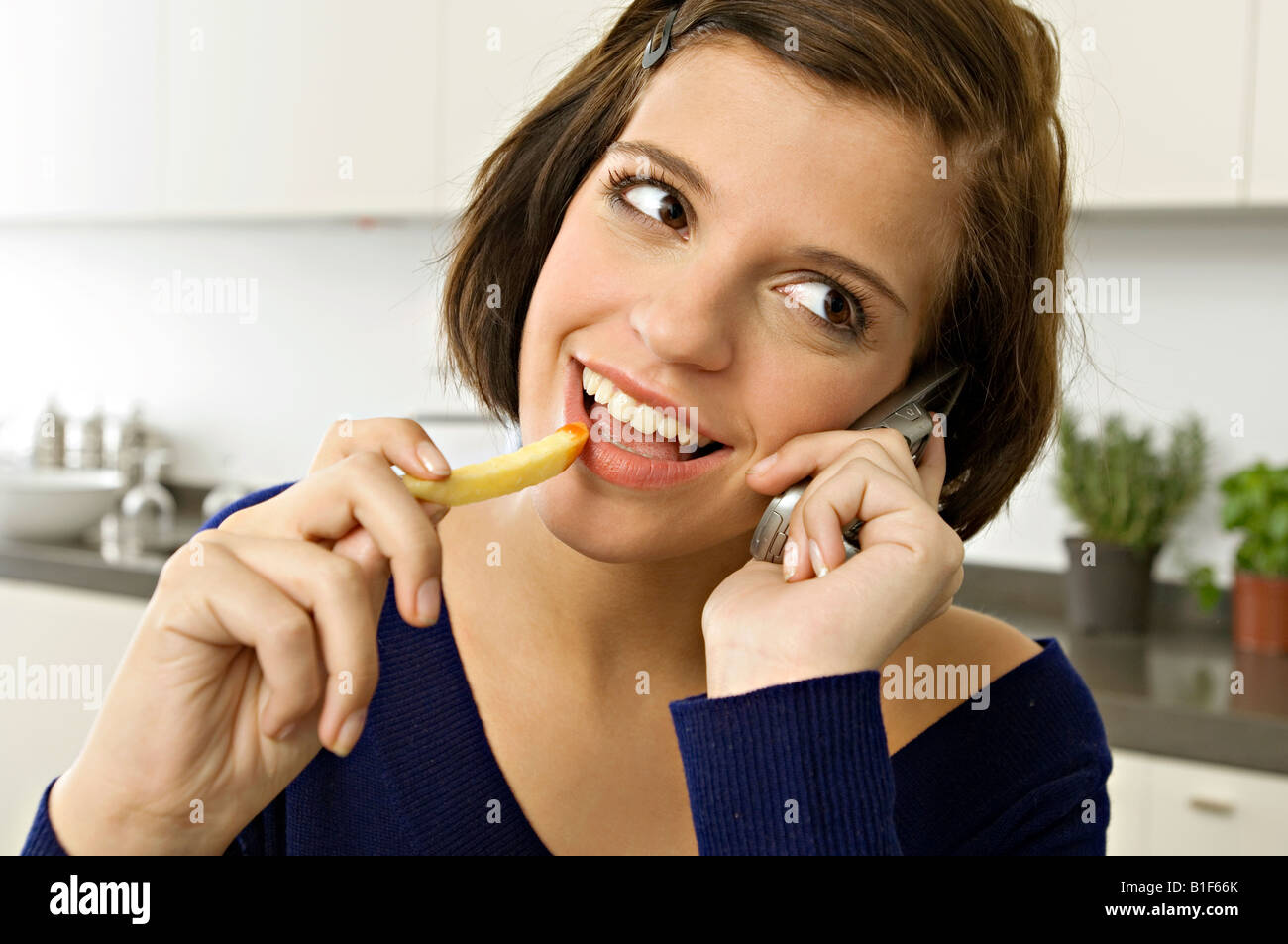 Close-up of a young woman eating French fries and talking on a mobile ...