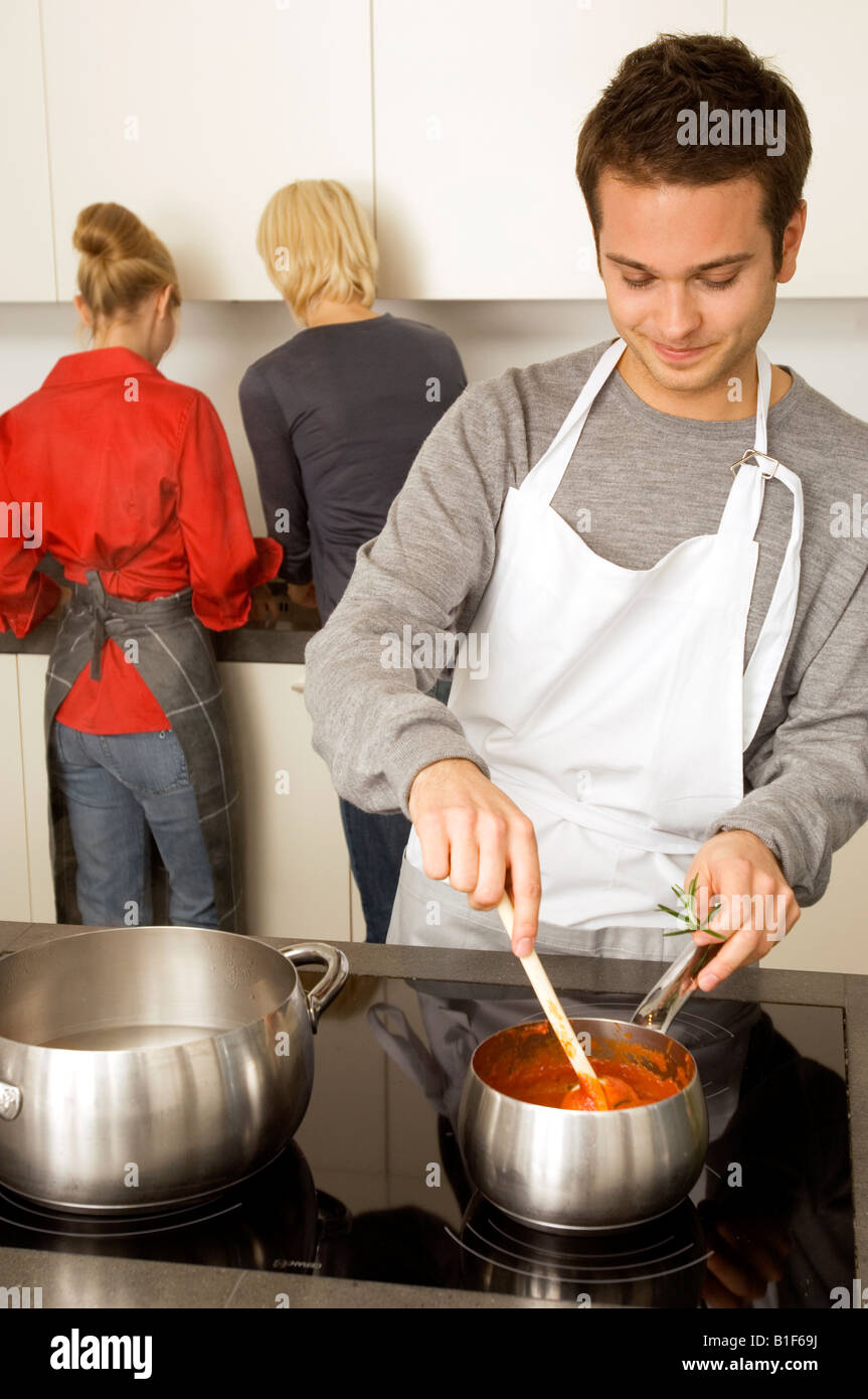Young man cooking food and two young women standing behind him in the ...