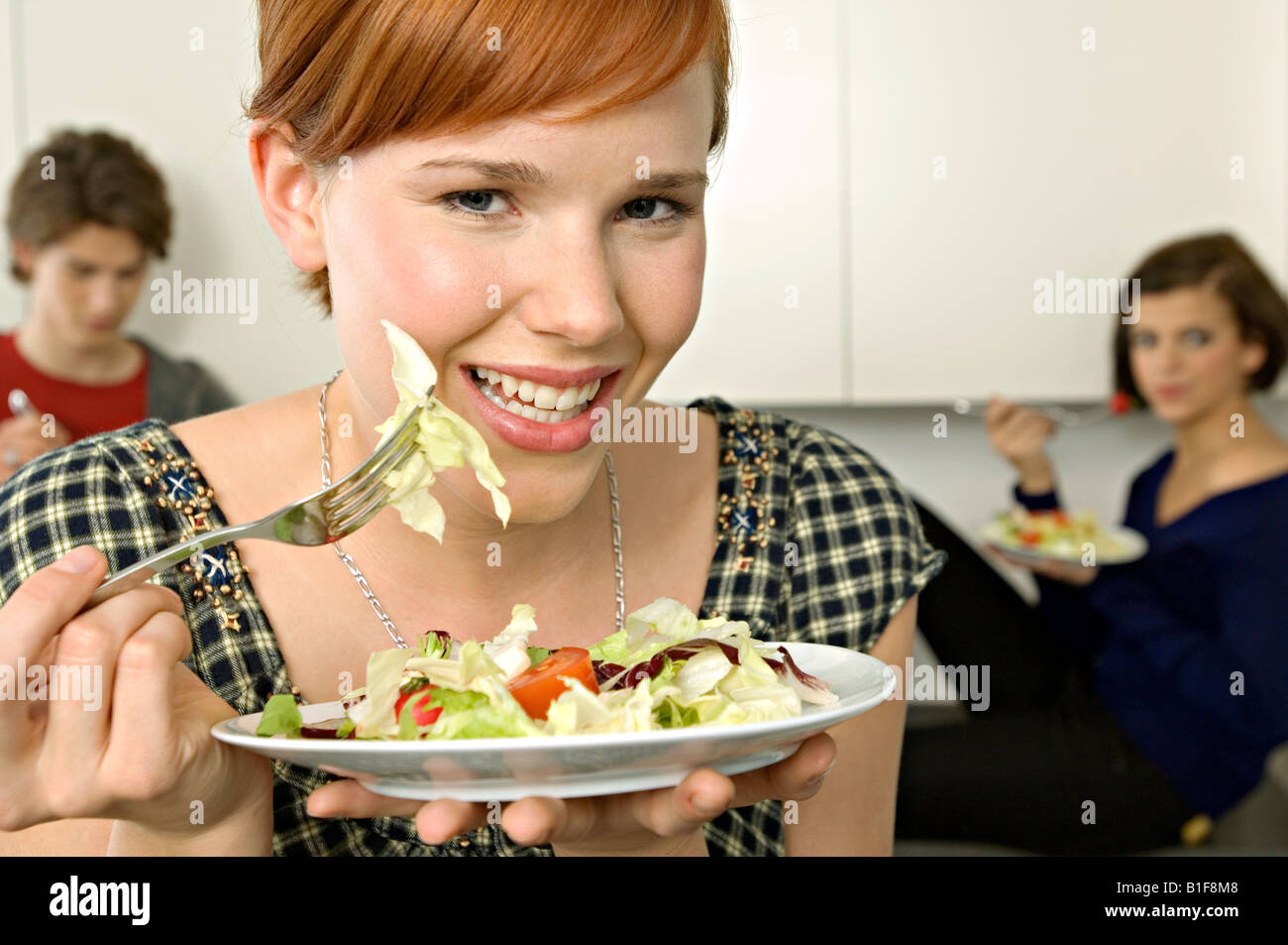 Portrait of a young woman eating salad with her friends in background ...
