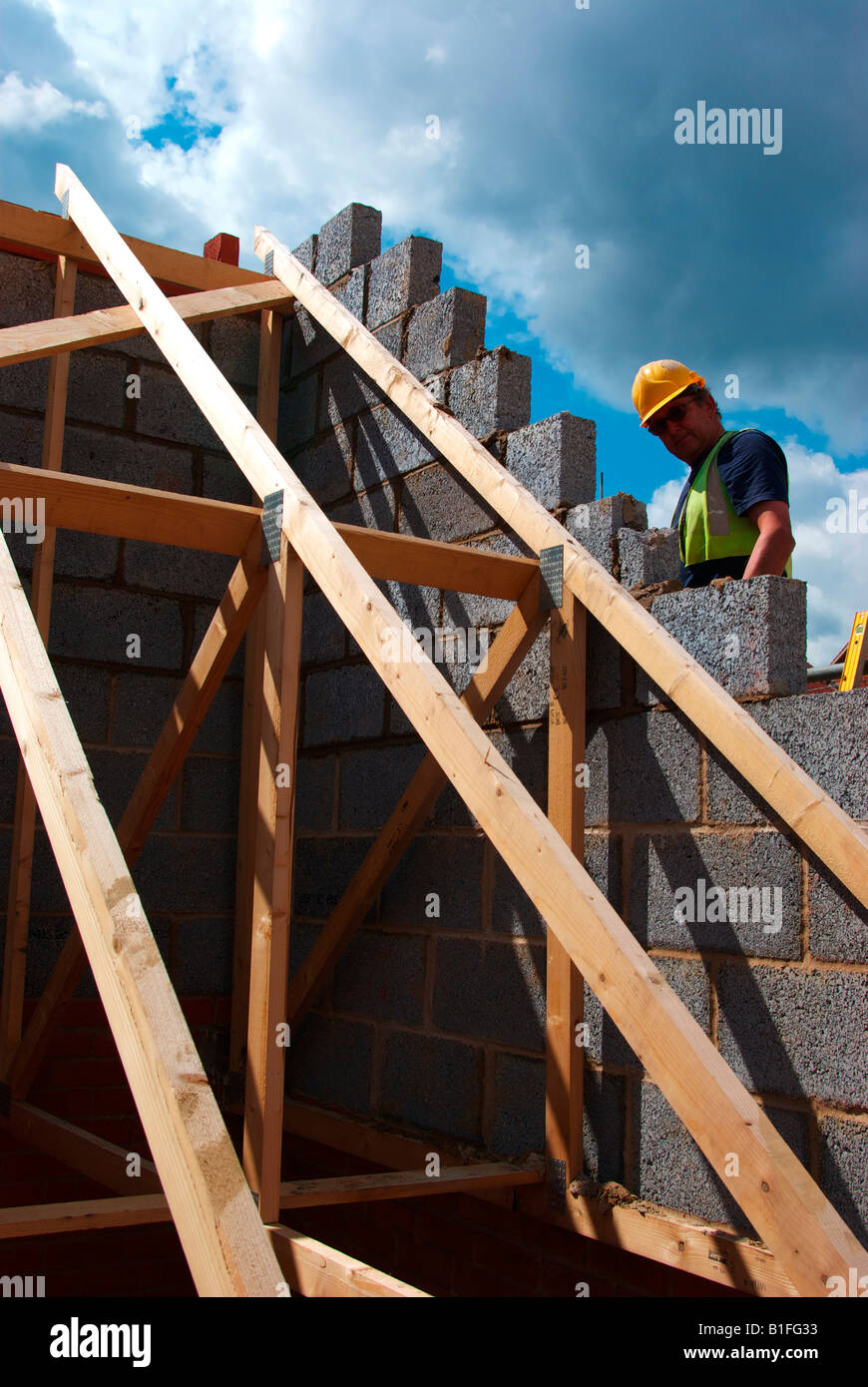 Bricklayer posing next to truss rafter on gable end, on large housing ...