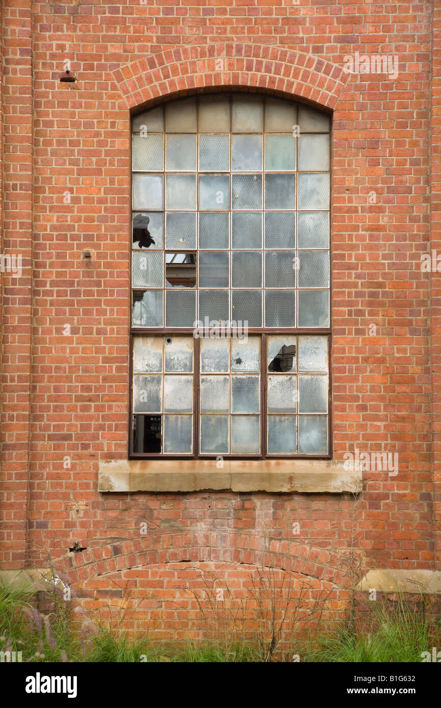 old arch style window frame in red brick wall with broken glass panes ...