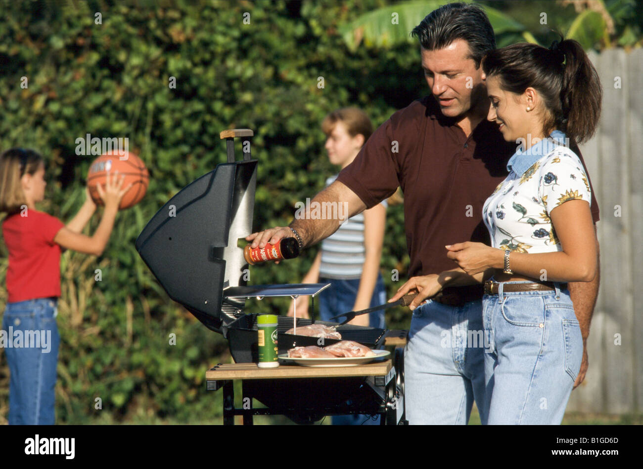Family cooking BBQ in back yard, with kids playing basketball Stock ...