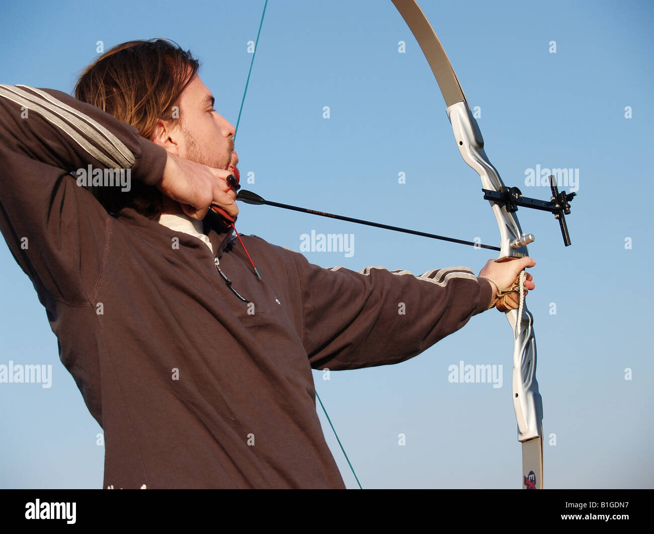 Side view of a young man aiming with bow and arrow Stock Photo - Alamy
