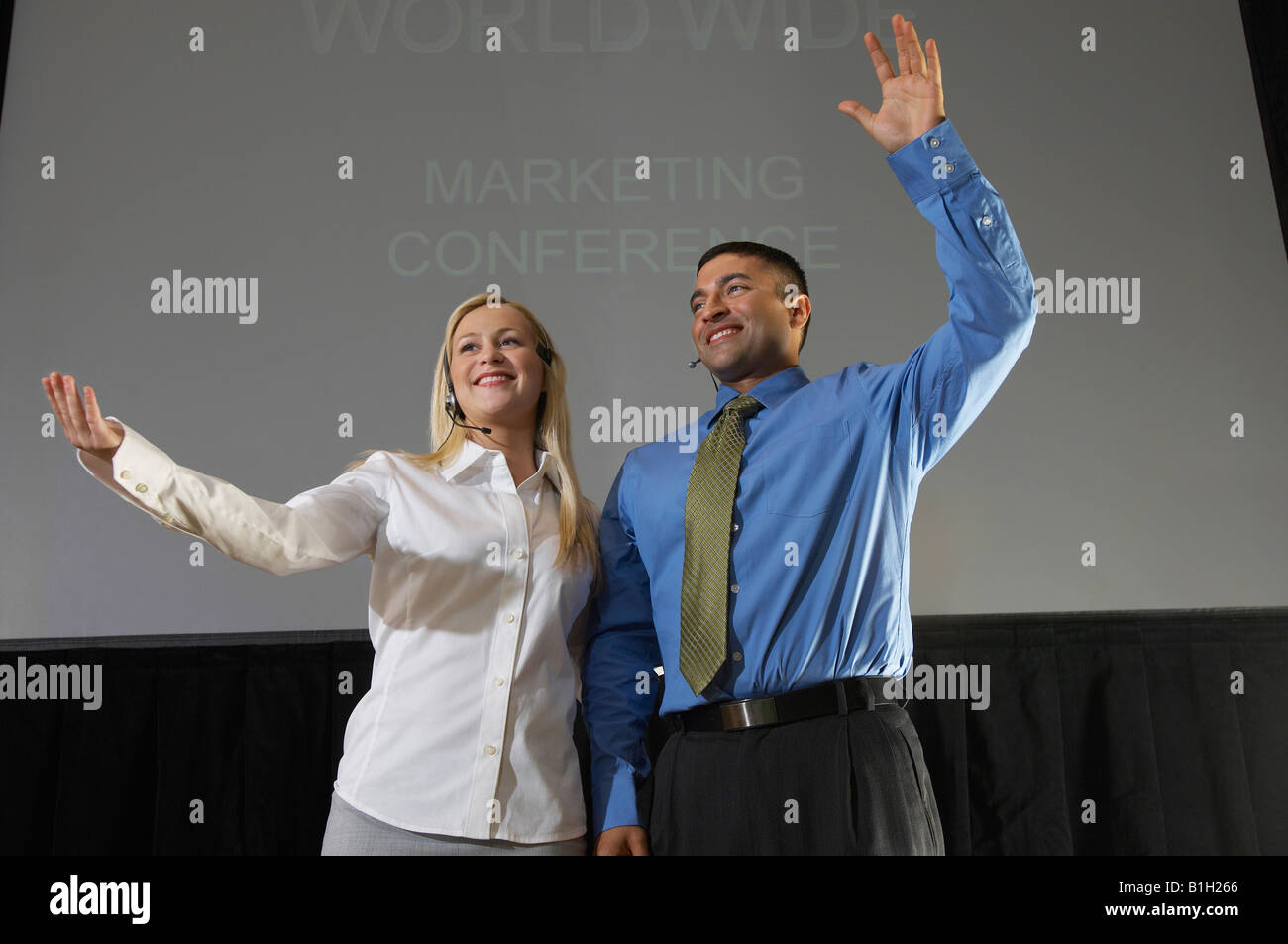Man and woman waving from stage during business convention Stock Photo ...