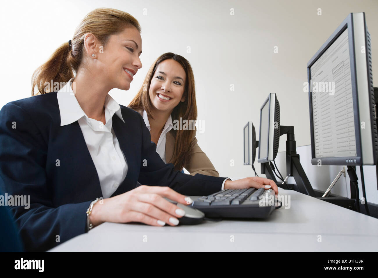 Two businesswoman smiling over computers on table Stock Photo - Alamy