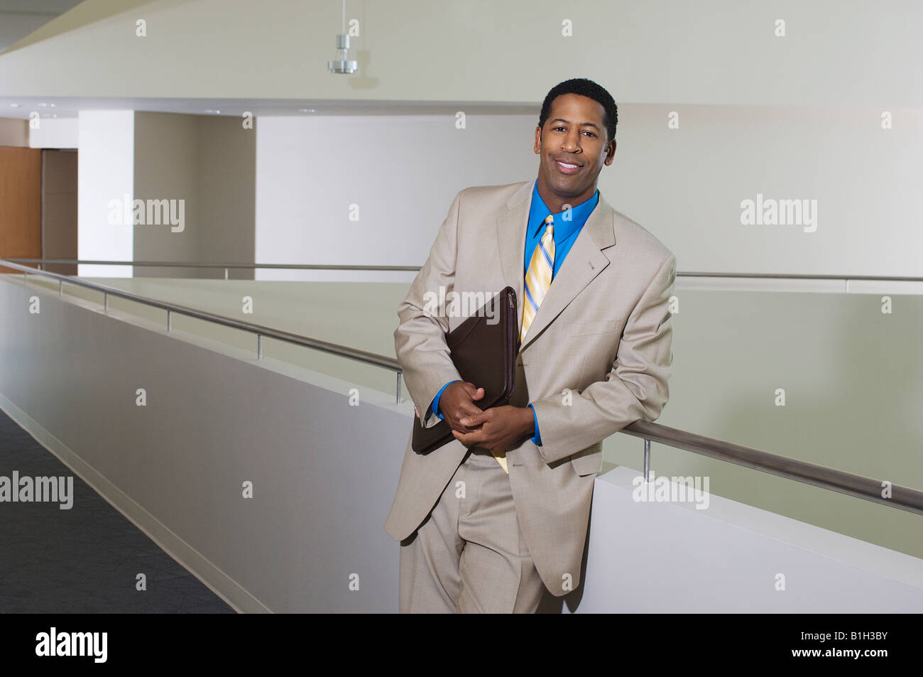 Business man standing by balustrade in office building, portrait Stock ...