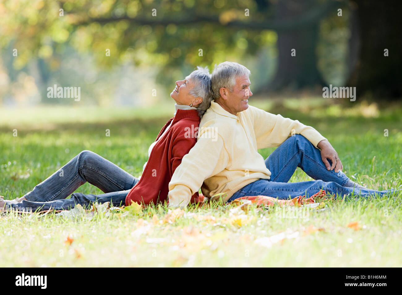 Senior couple sitting back to back in a park Stock Photo - Alamy