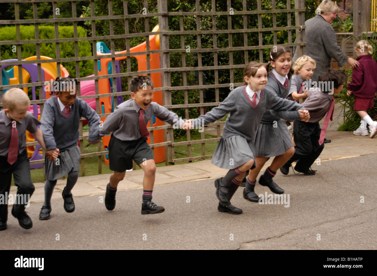 children in a line holding hands running in the playground of school ...