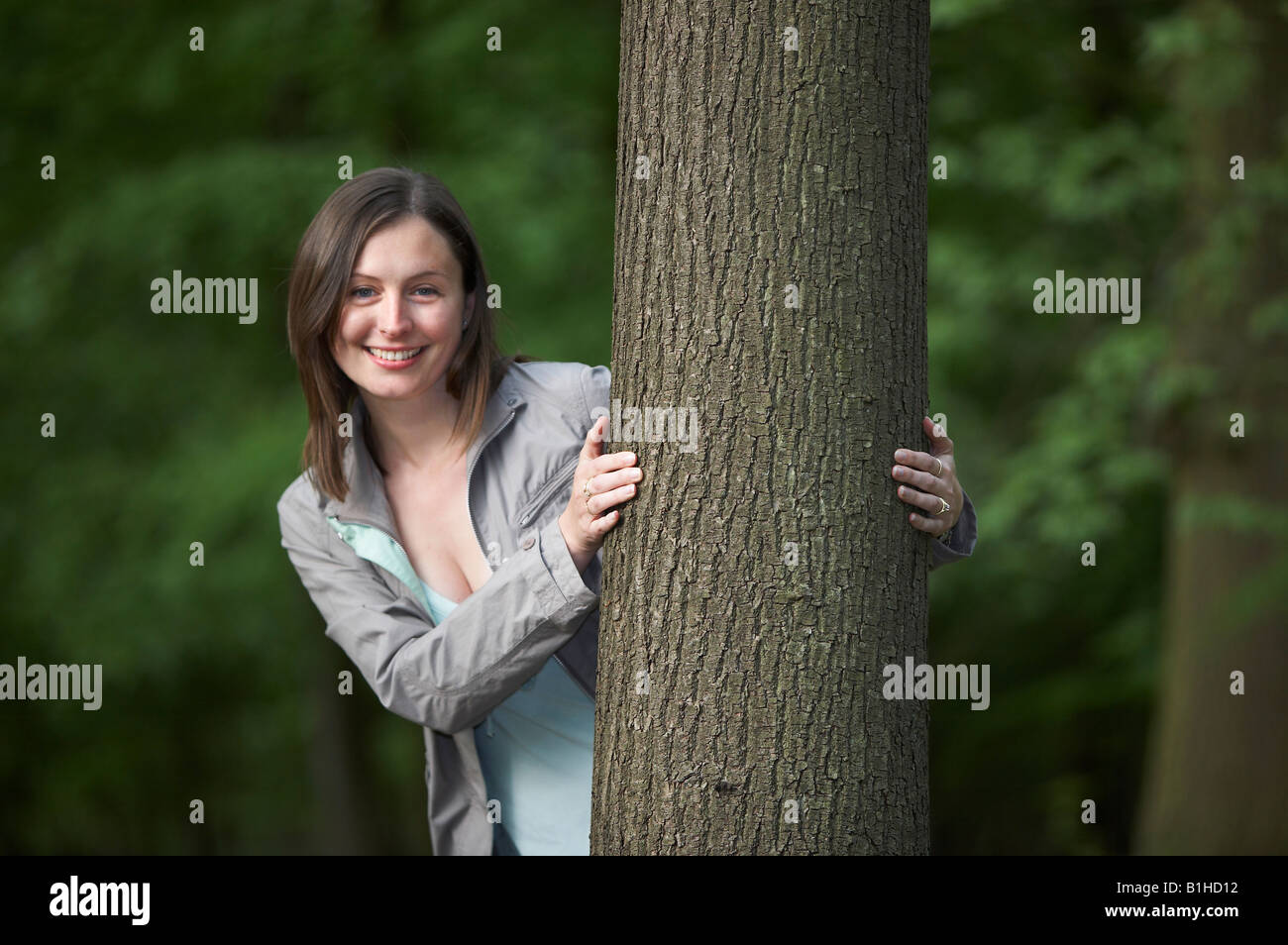 Young woman hiding behind tree Stock Photo - Alamy