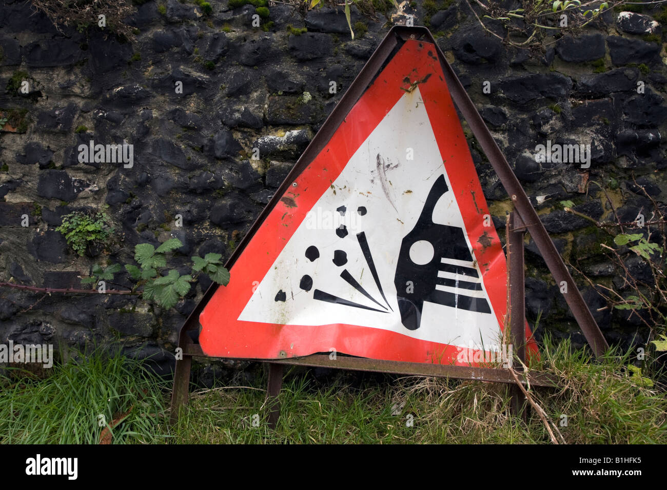 Damaged road warning sign against a stone wall in the village of Castle ...