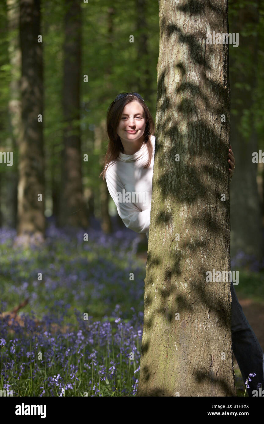 Young woman hiding behind a tree in Bluebell wood Stock Photo - Alamy
