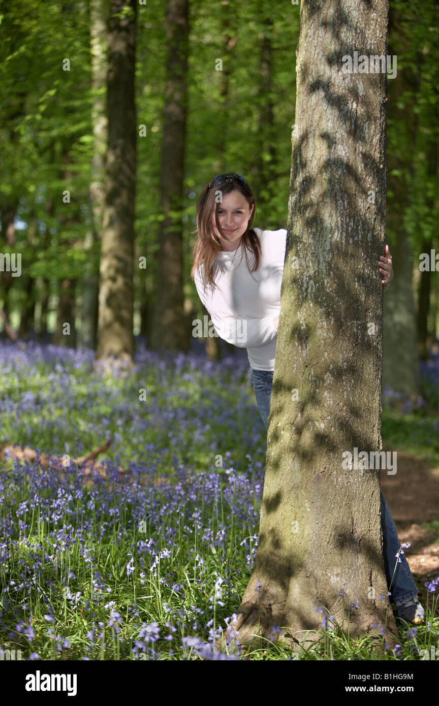 Young woman hiding behind a tree in Bluebell wood Stock Photo - Alamy