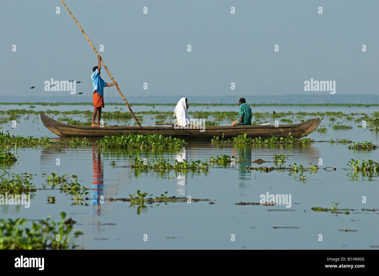 Indian man using a pole to propel canoe with another man and woman ...