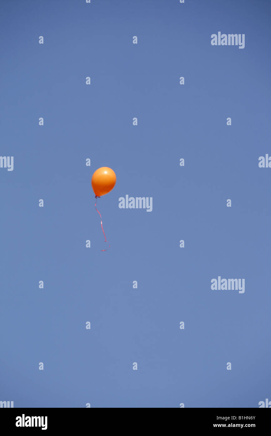 one orange balloon floating up in blue sky Stock Photo - Alamy