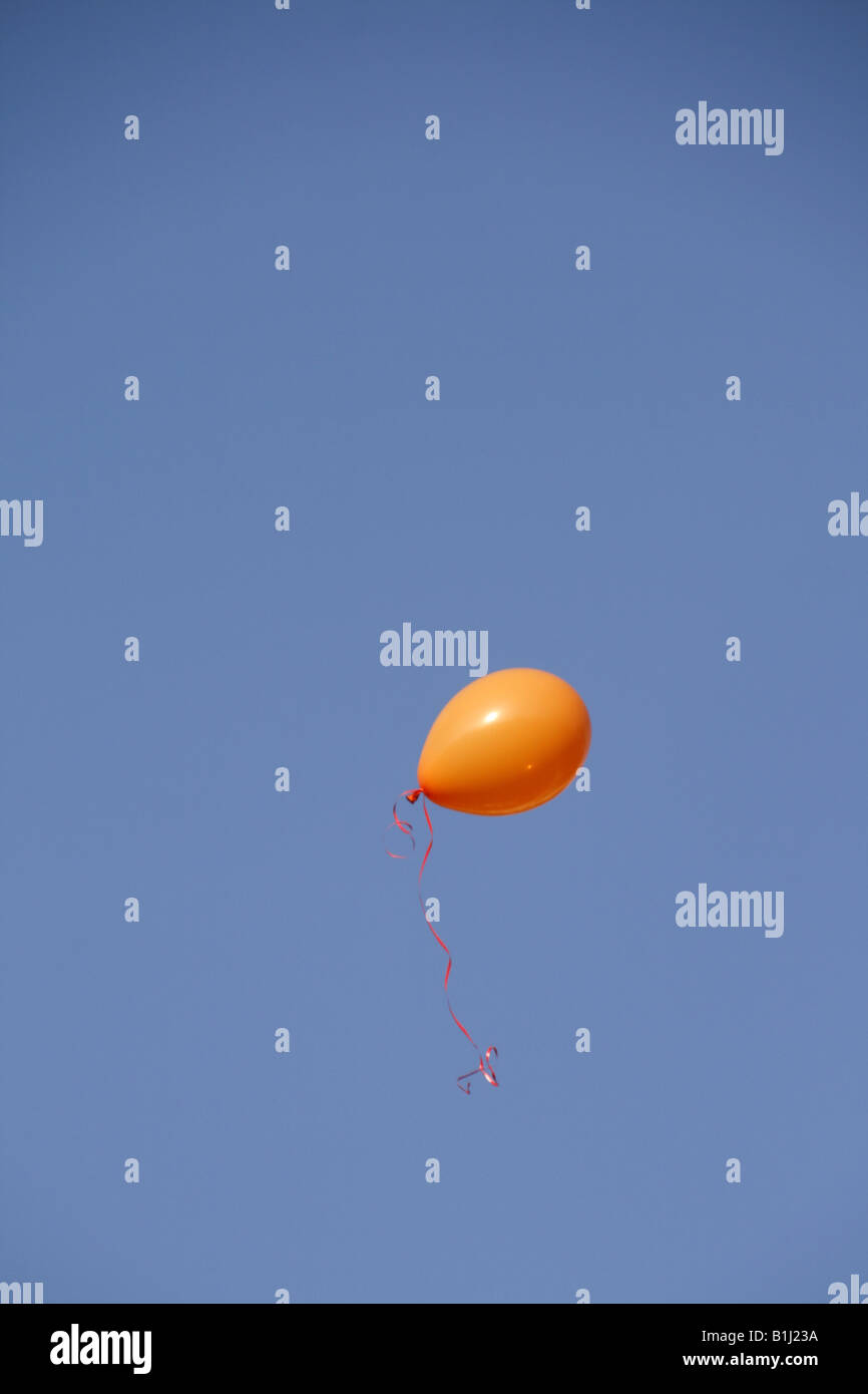 one single orange balloon floating in blue sky Stock Photo - Alamy