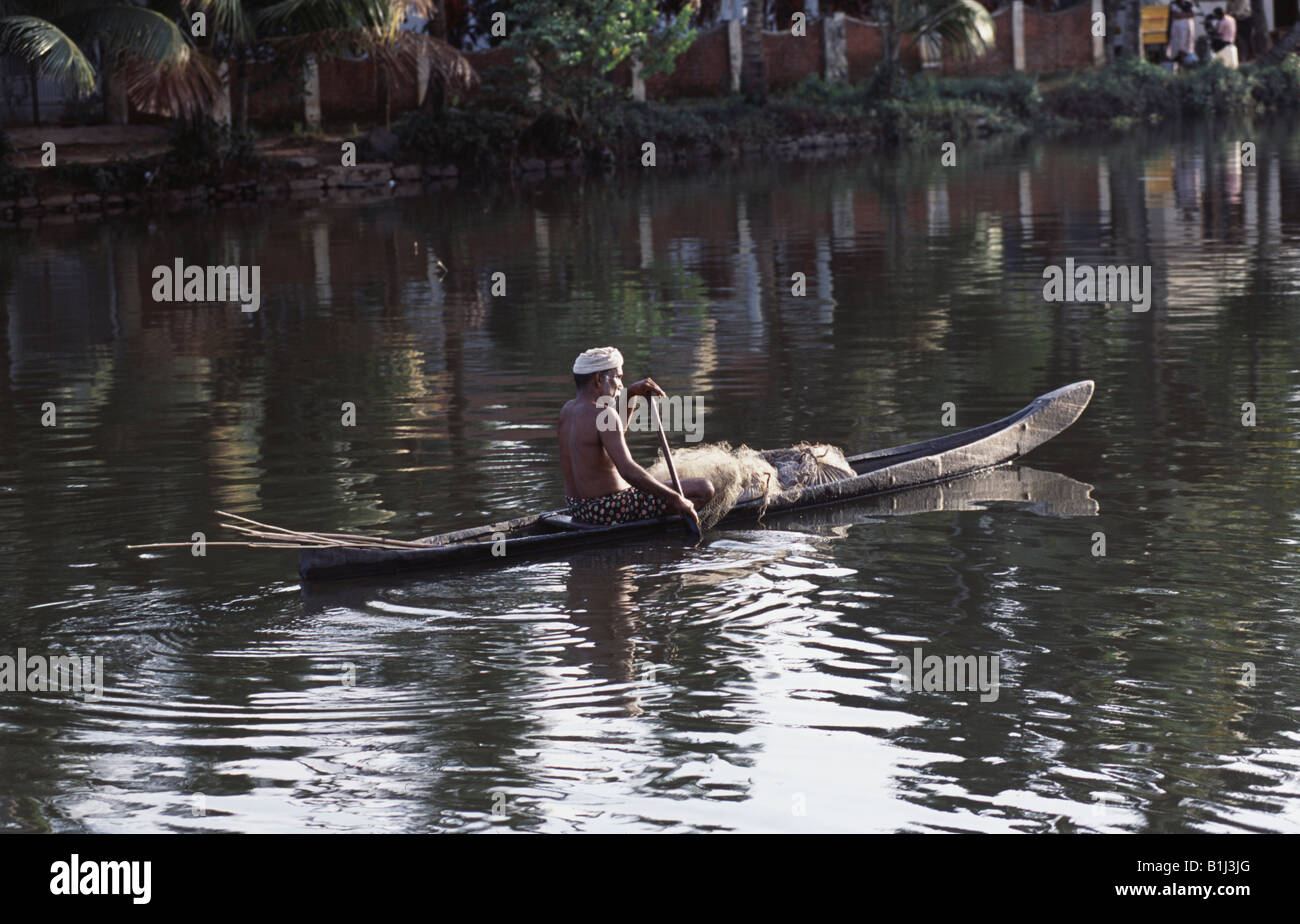 Rear view of a fisherman rowing a boat in a lake, Kerala Backwaters ...