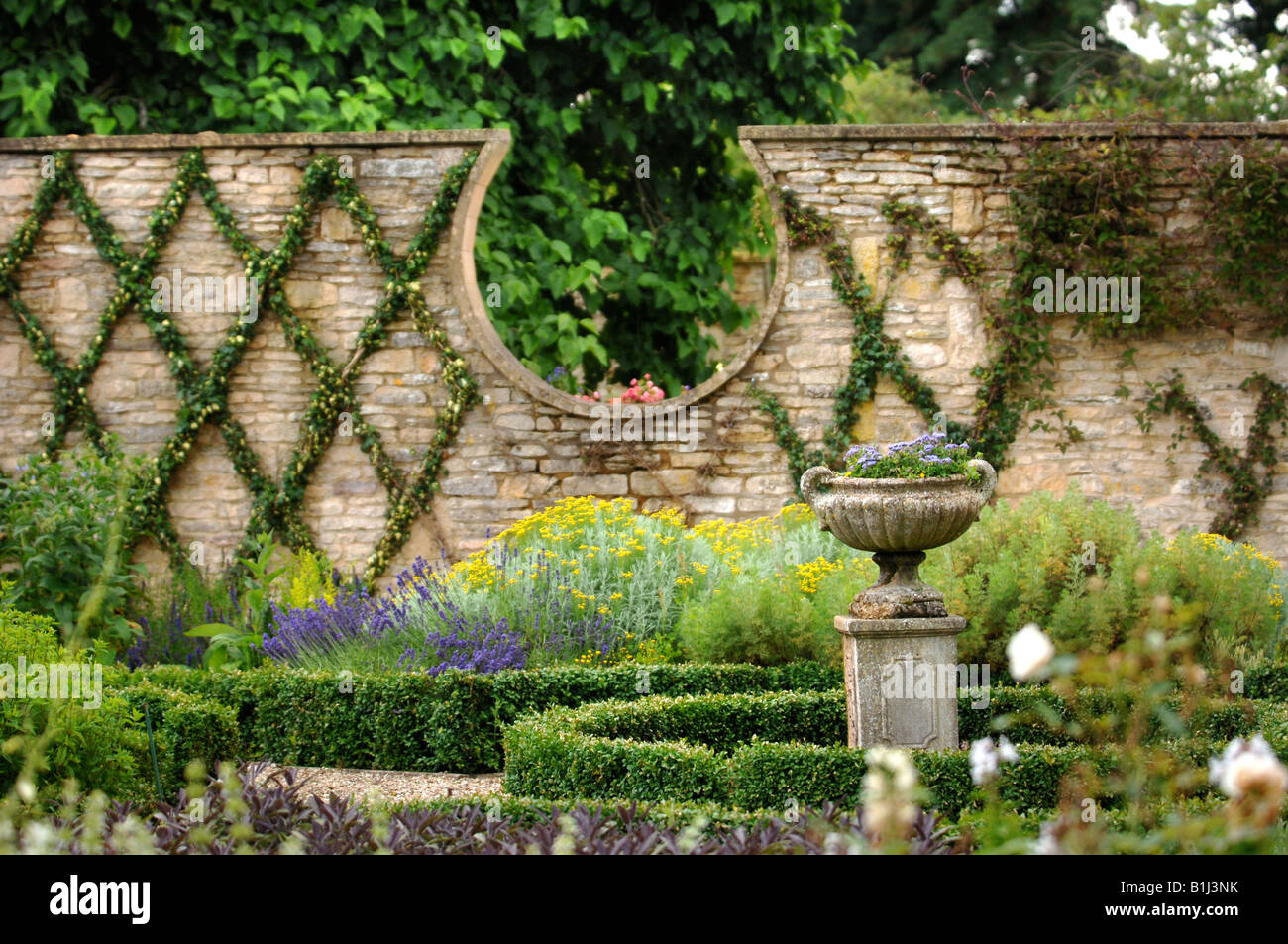 AN ANTIQUE STONE URN IN A WALLED GARDEN WITH DWARF BOX HEDGING AND AN ...
