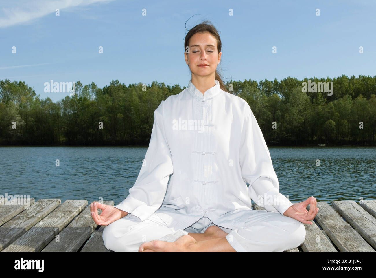young pretty woman practising Yoga on a boardwalk at a lake, Muktasana ...