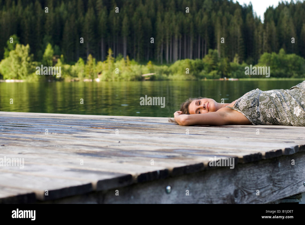 young cute woman in summer dress, lying on a footbridge at a swimming ...