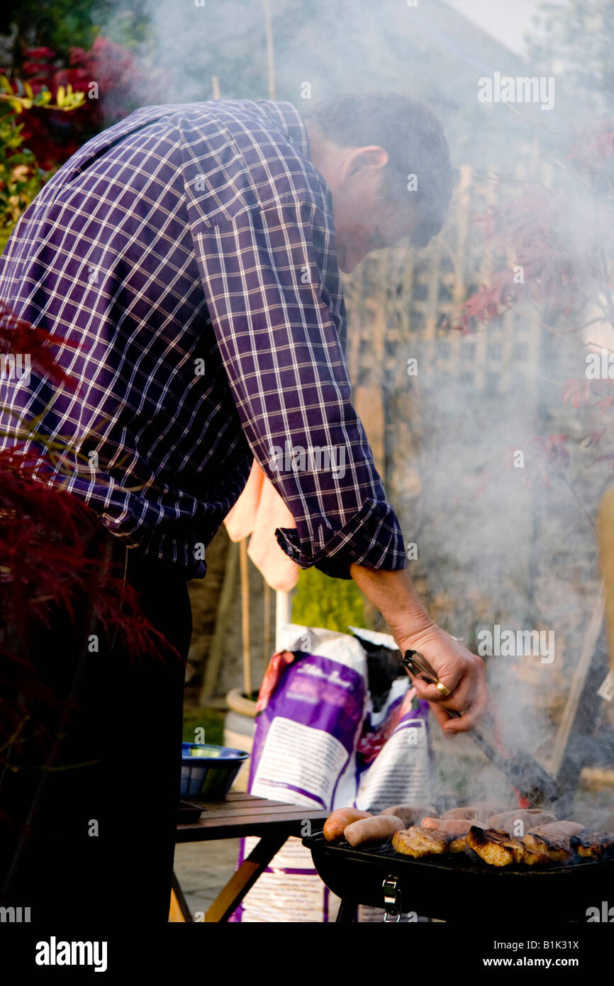 Mature man cooking meat with a smoking barbecue in a garden setting ...