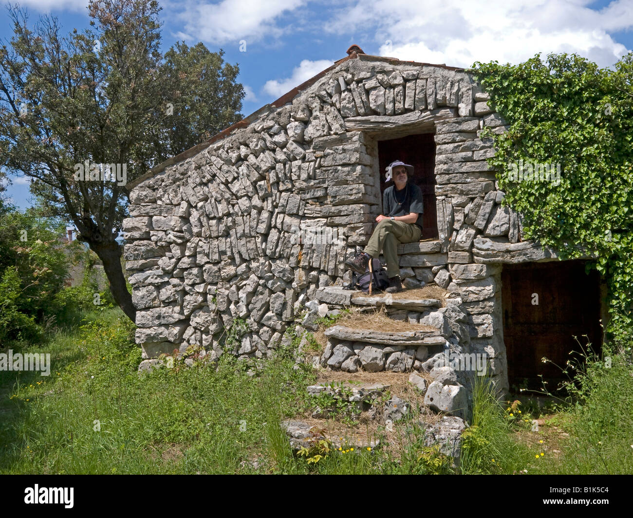 bearded middle aged man hiking having a pause at an old stony cottage ...