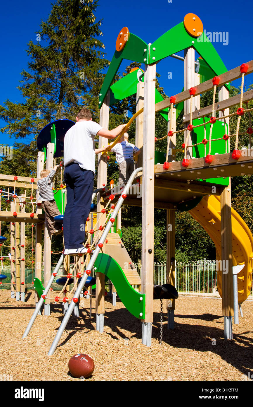 Father watching his children play on adventure playground equipment ...