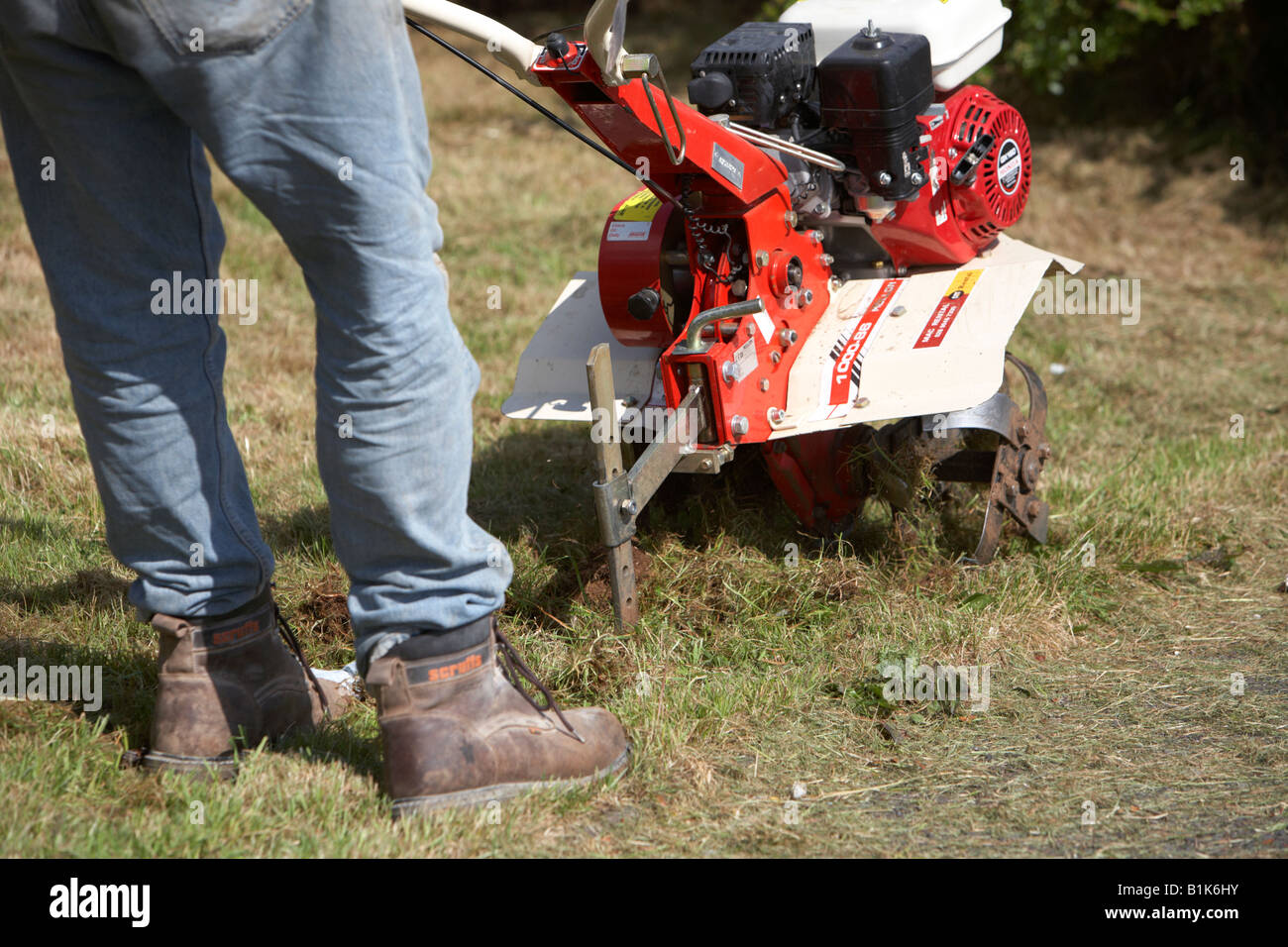 man wearing jeans and safety boots operates petrol driven garden ...