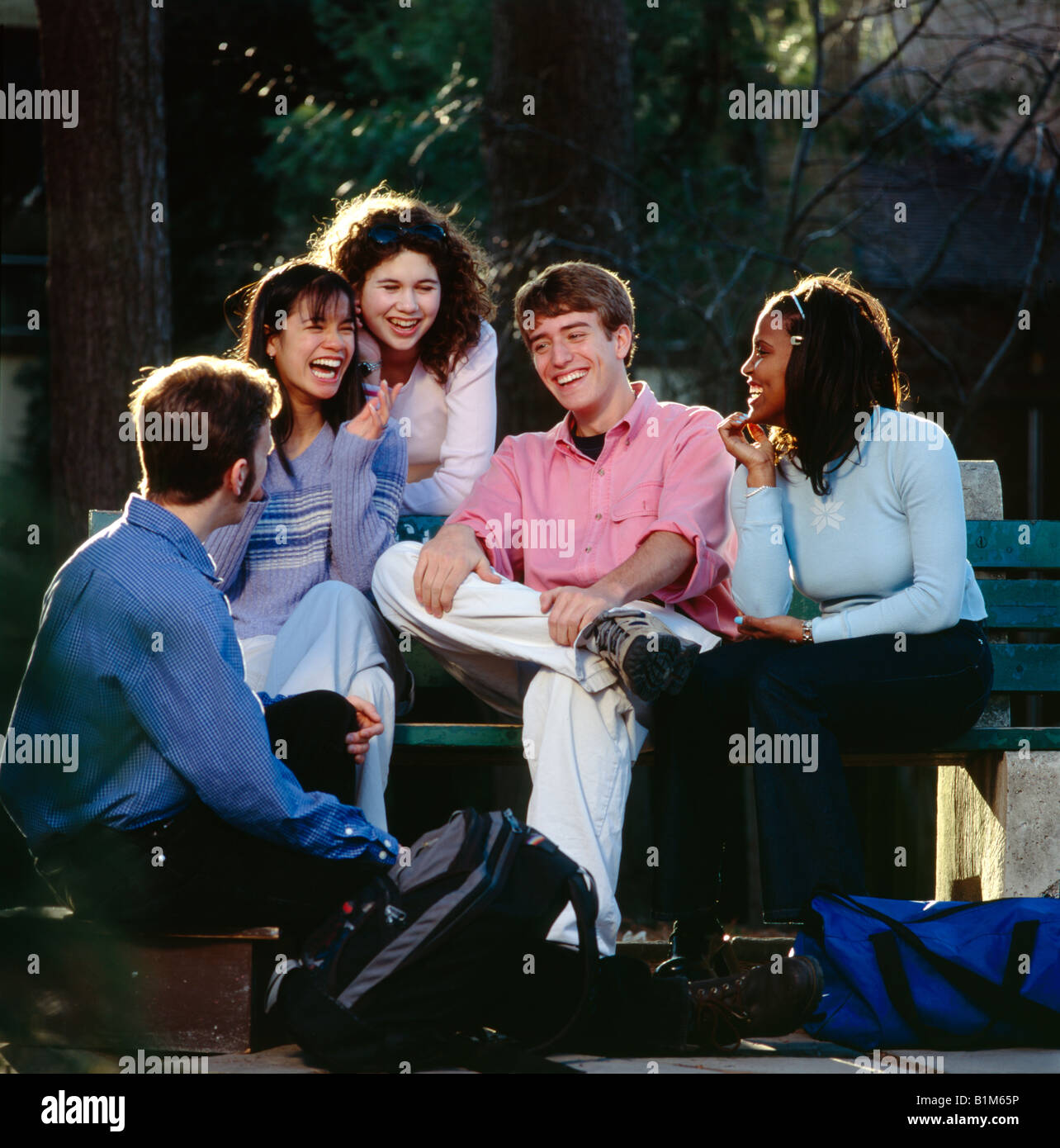 High school students talking and laughing outside on a campus bench ...