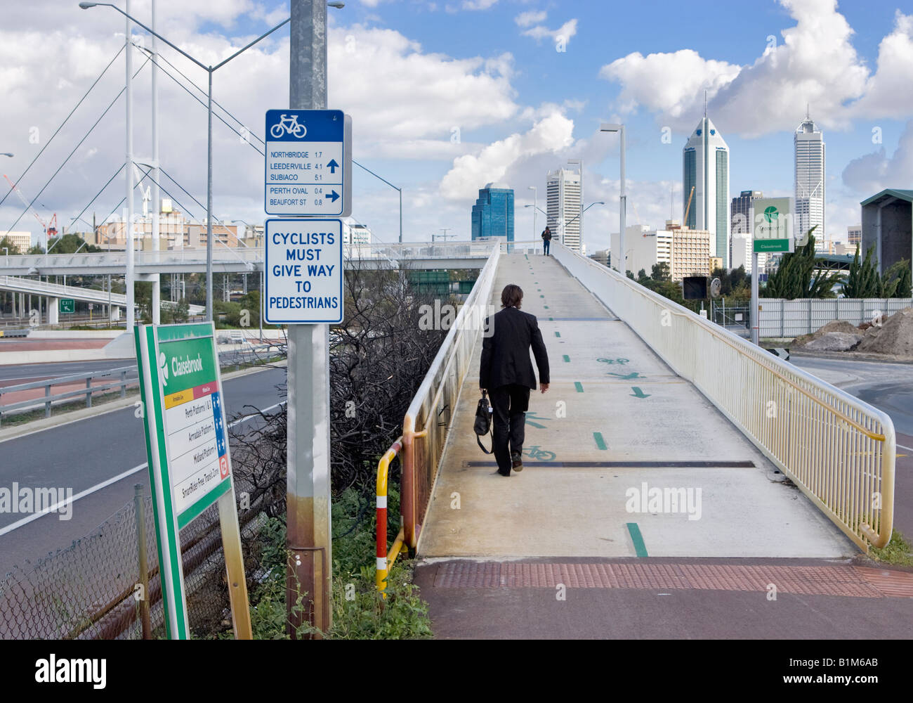 A suited man with a briefcase walking up an overpass with skyscrapers ...