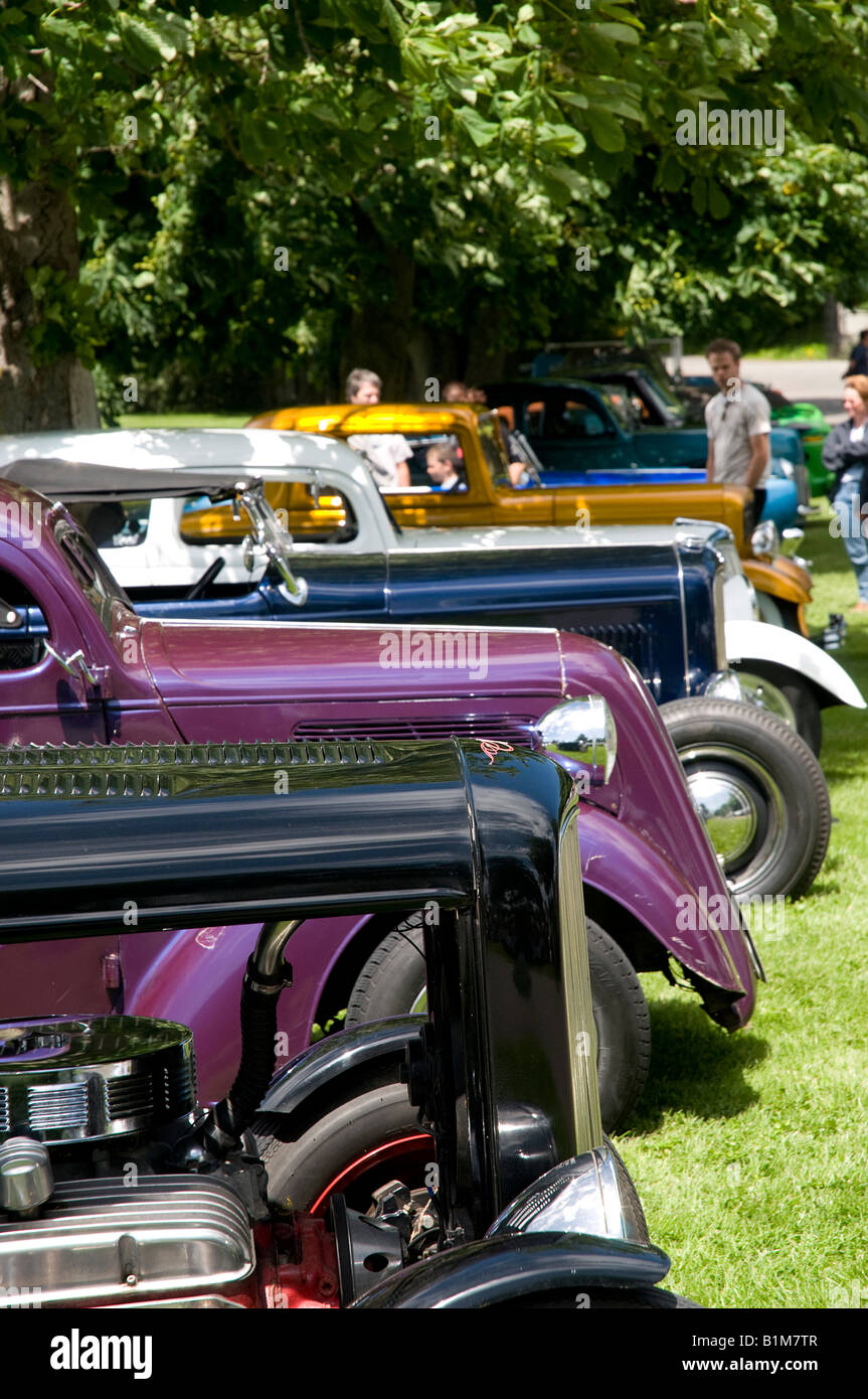 looking across the fronts of a row of parked custom cars at a rally in ...