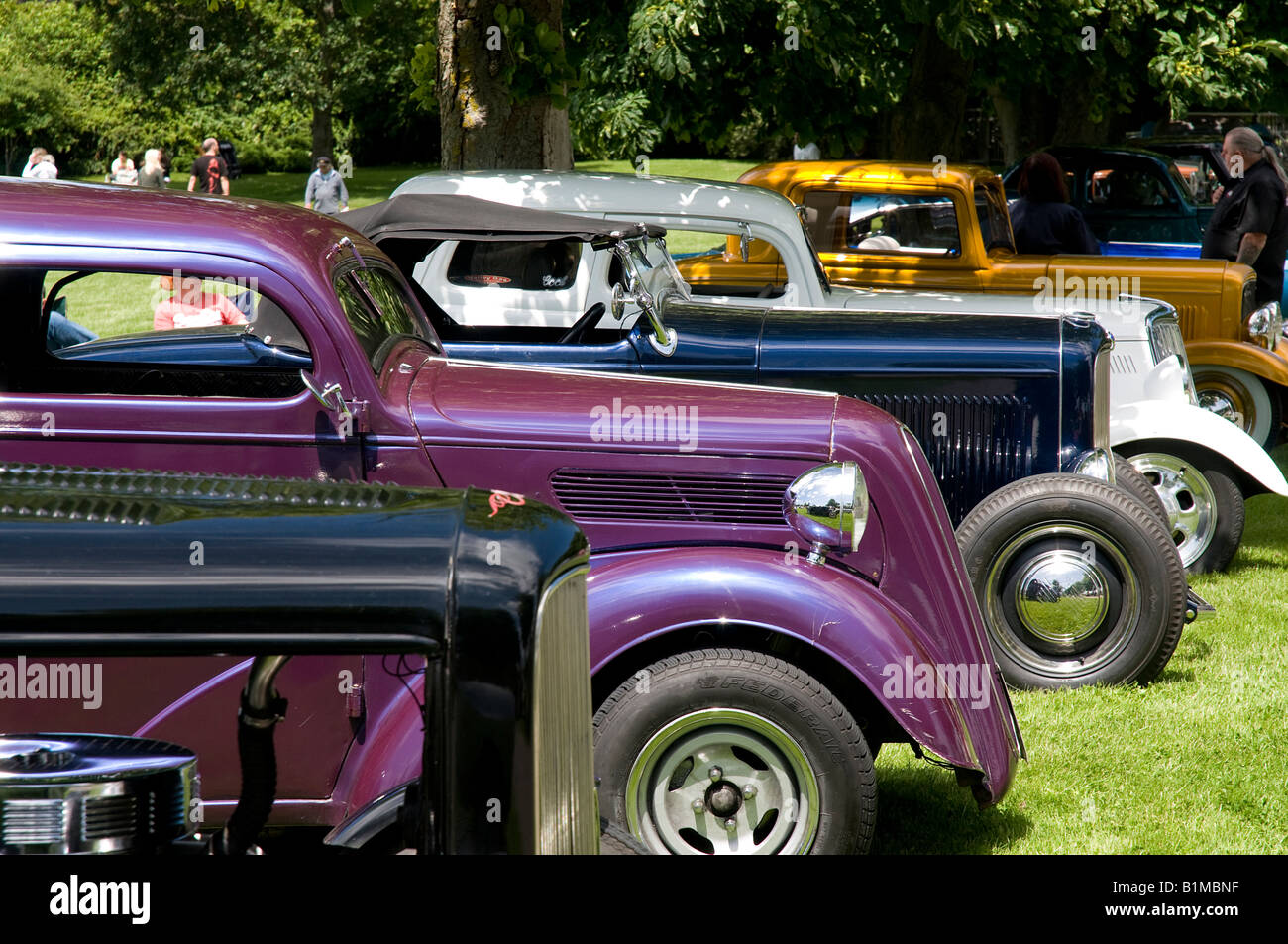 looking across the fronts of a row of parked custom cars at a rally in ...